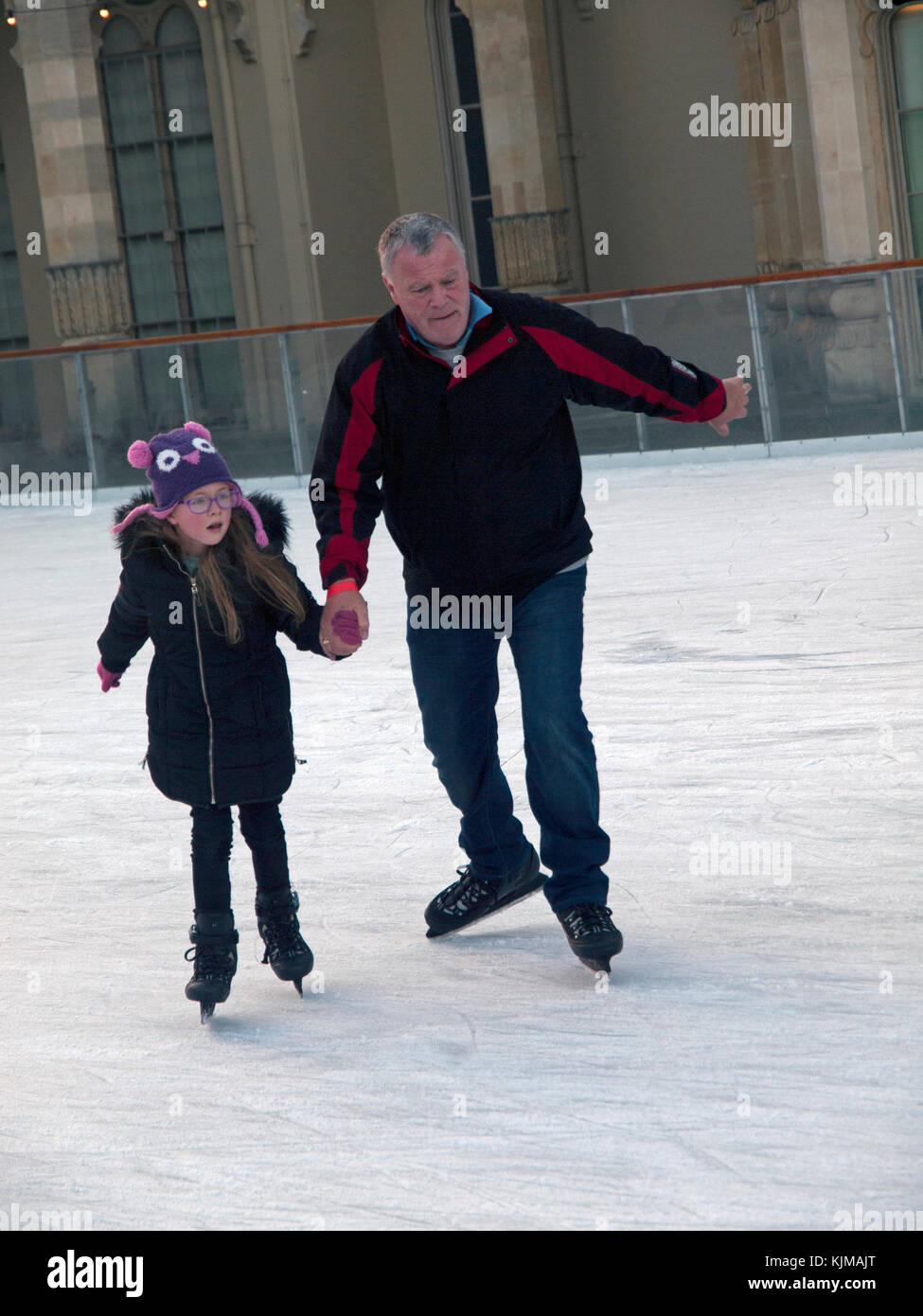 A child and an adult hold hands while skating on an ice rink in ...