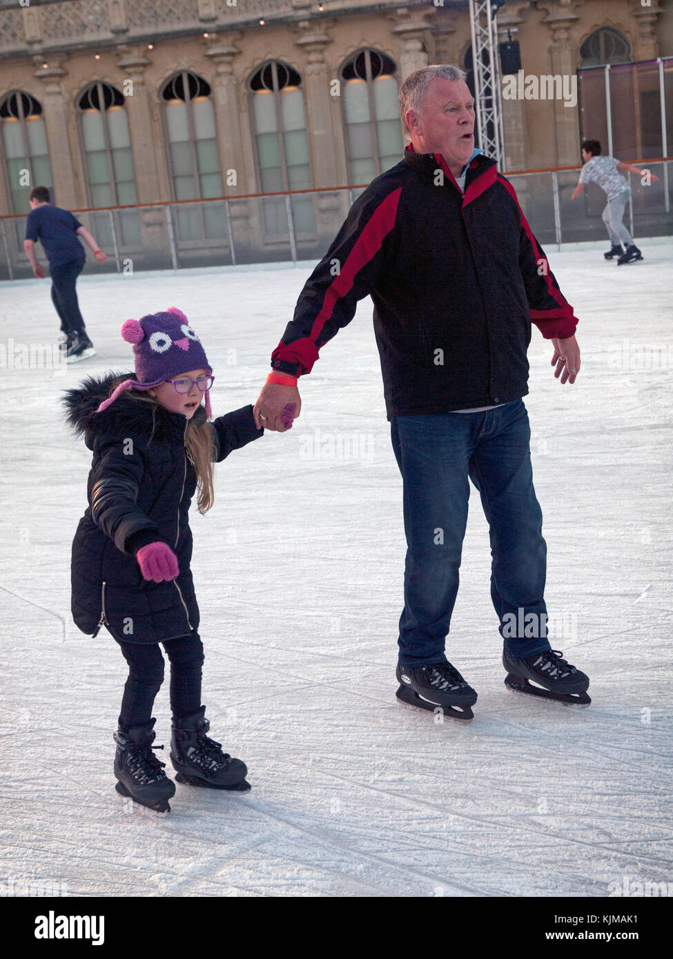 A child and an adult hold hands while skating on an ice rink in ...