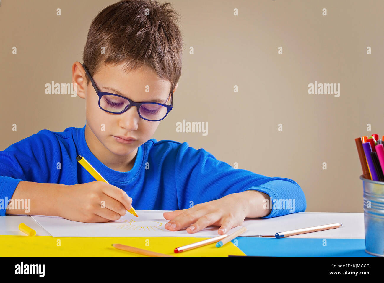 Focused boy with glasses drawing with colored pencils and felt pens ...