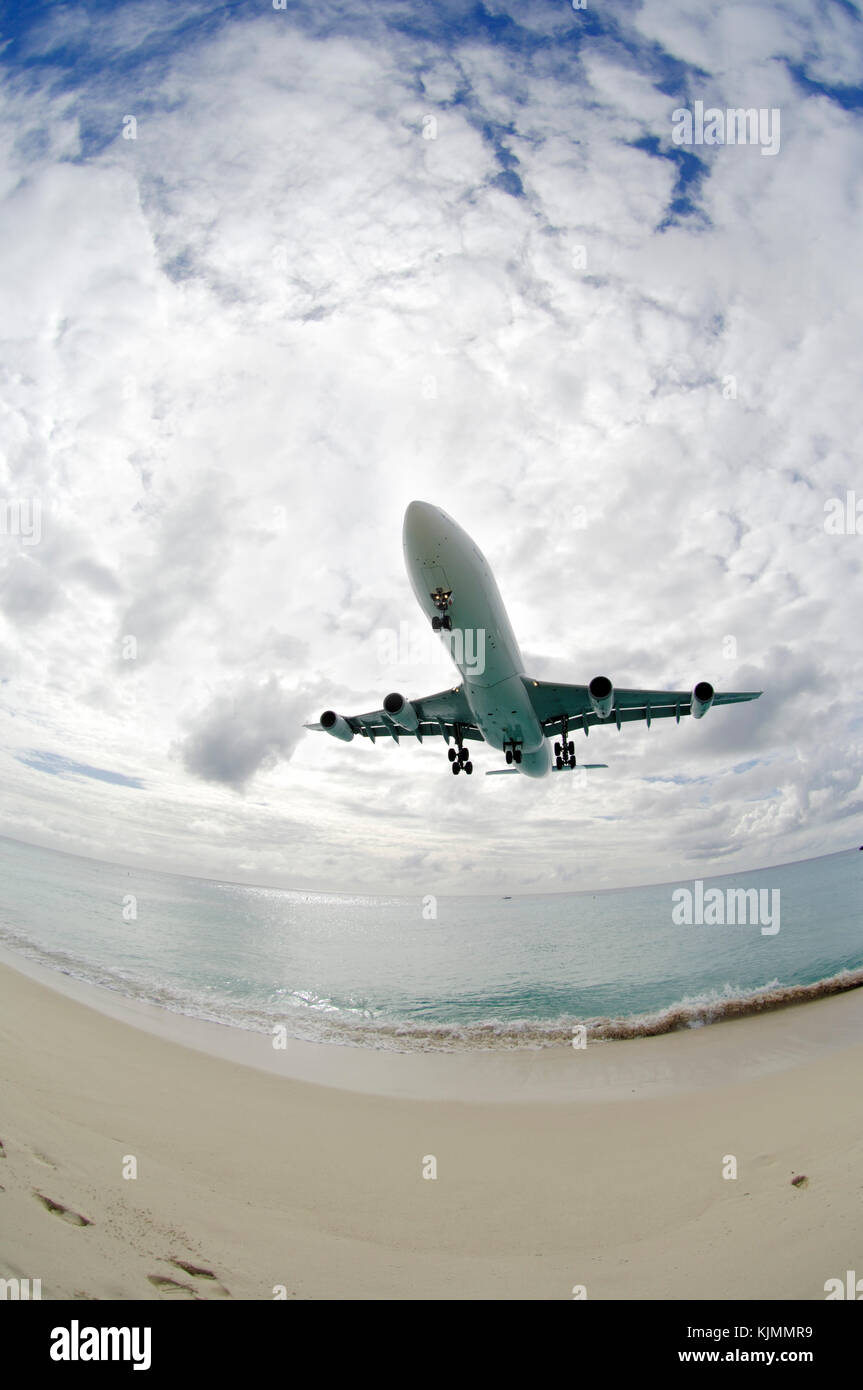 very low on final-approach landing over Maho Beach with clouds behind ...