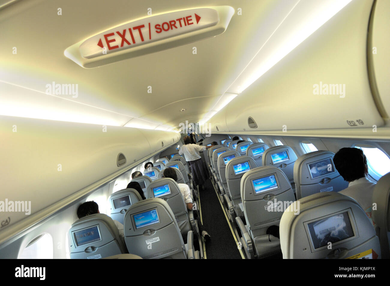 exit sign with passengers standing in the aisle of the Embraer 190 ...