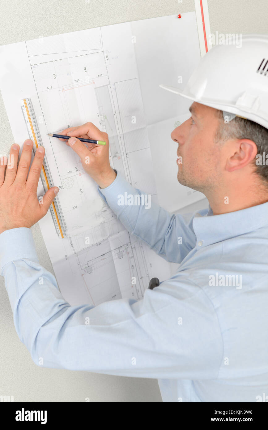 Man measuring plans pinned to wall Stock Photo - Alamy