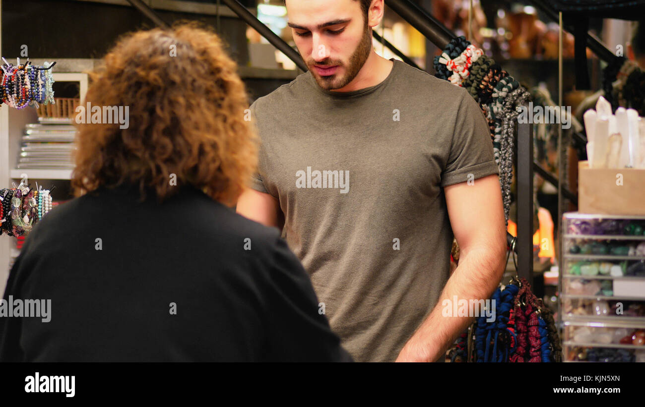 Young man working in shop and talking to customer giving some help ...
