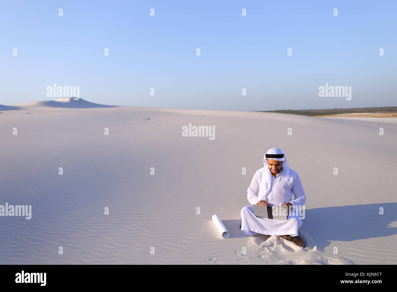 Muslim male architect sitting with laptop on sand in desert on h Stock ...