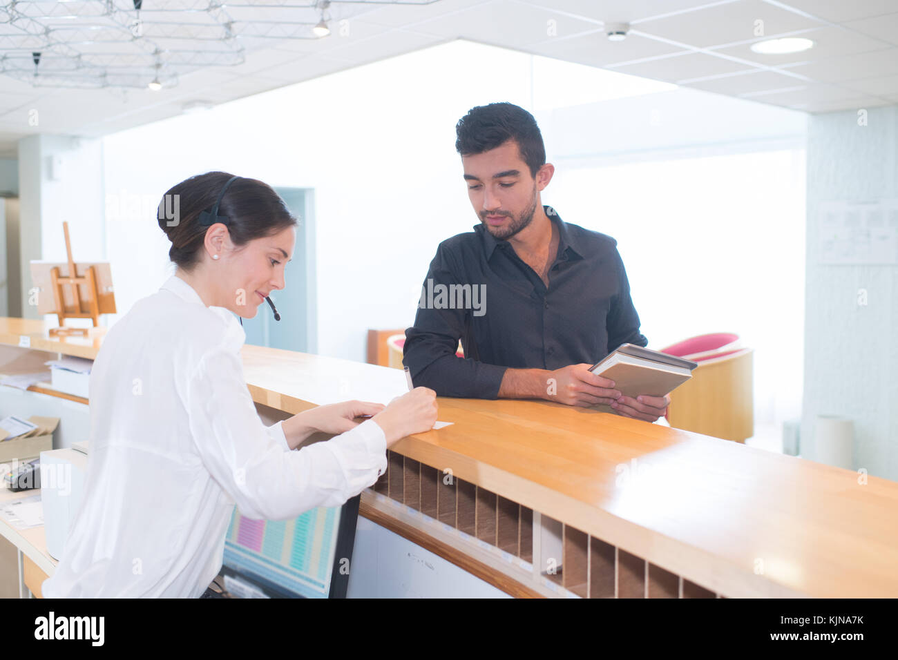 Receptionist making note for man Stock Photo - Alamy