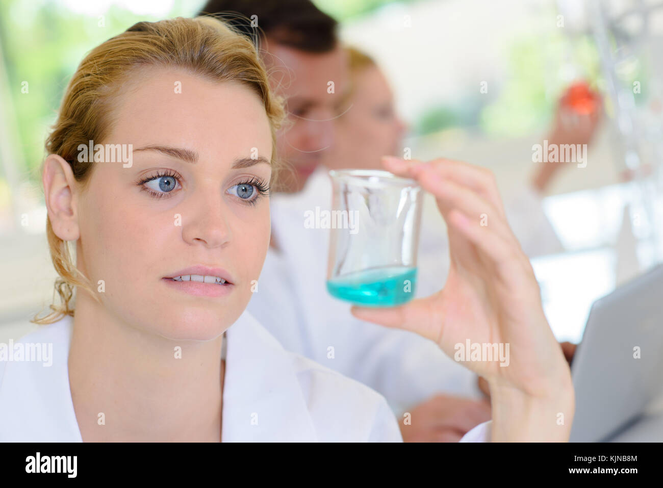 Female technician looking at liquid in glass beaker Stock Photo - Alamy