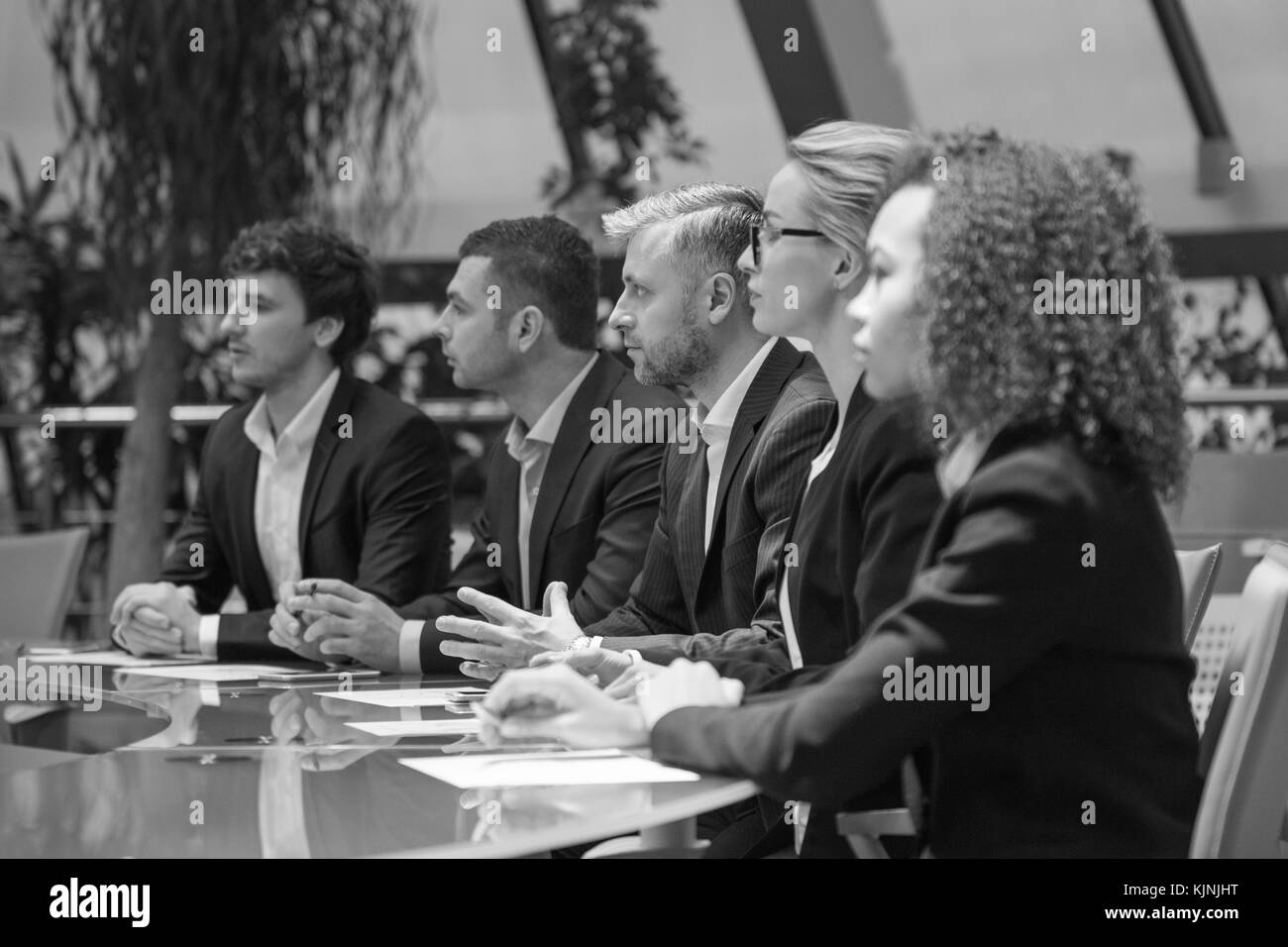 A group of business people sit at a table in a line and are discussing ...