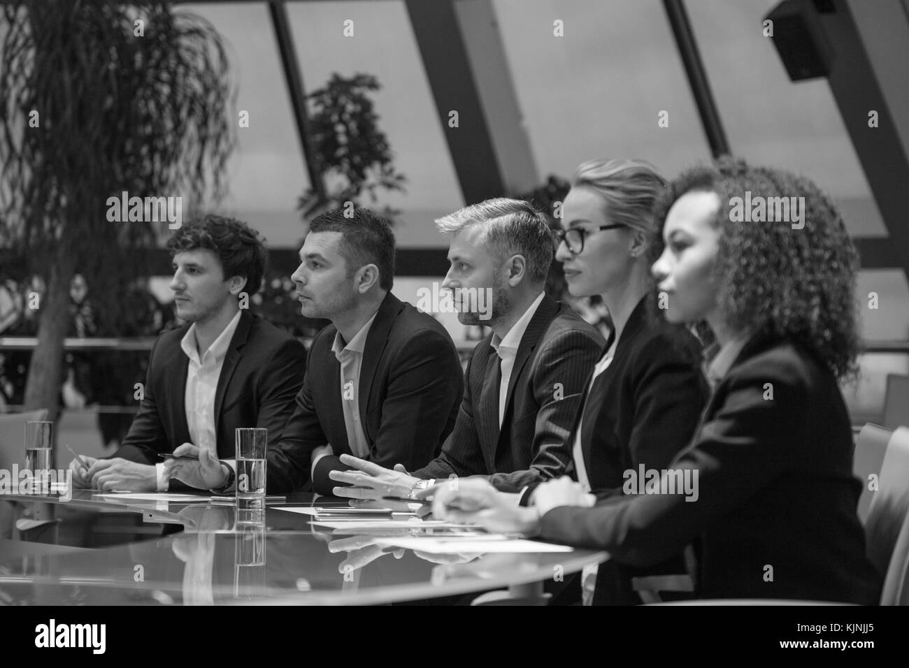 A group of business people sit at a table in a line and are discussing ...