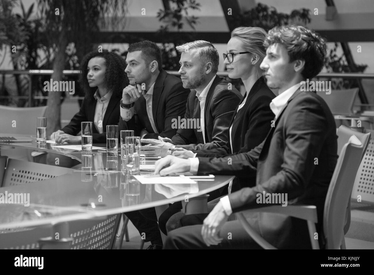 A group of business people sit at a table in a line and are discussing ...