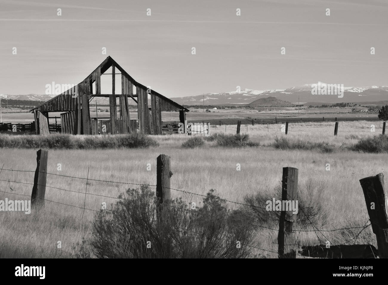 Old dilapidated wooden barn behind a fence with snow capped mountains ...