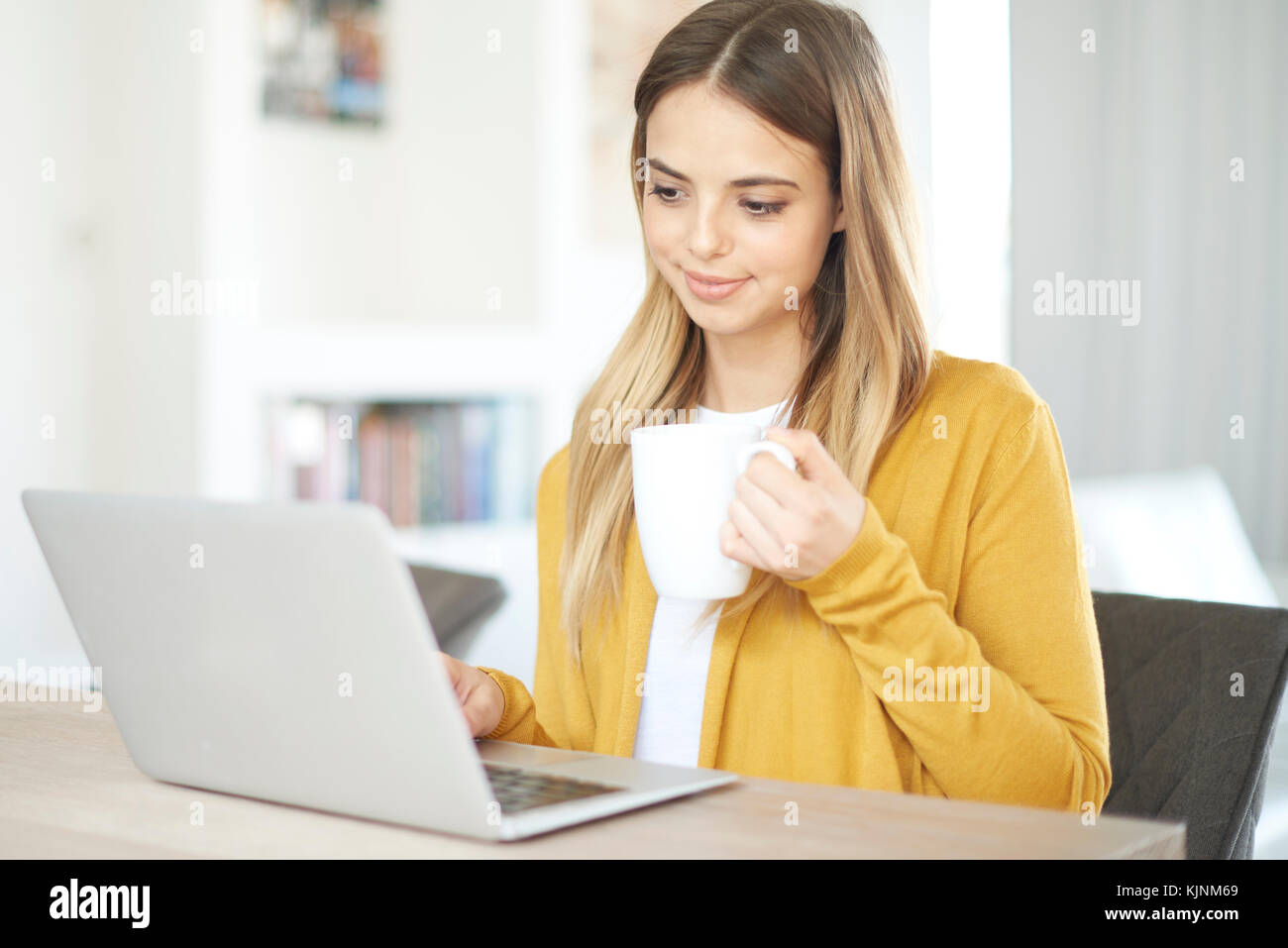 Shot of a young female student drinking tea while using working on ...
