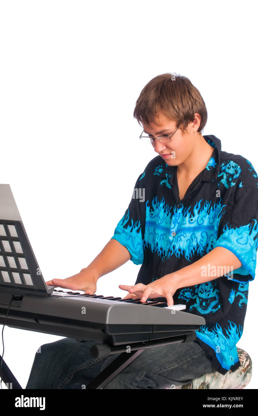 A teenage boy seated at a keyboard playing. Isolated against a white ...