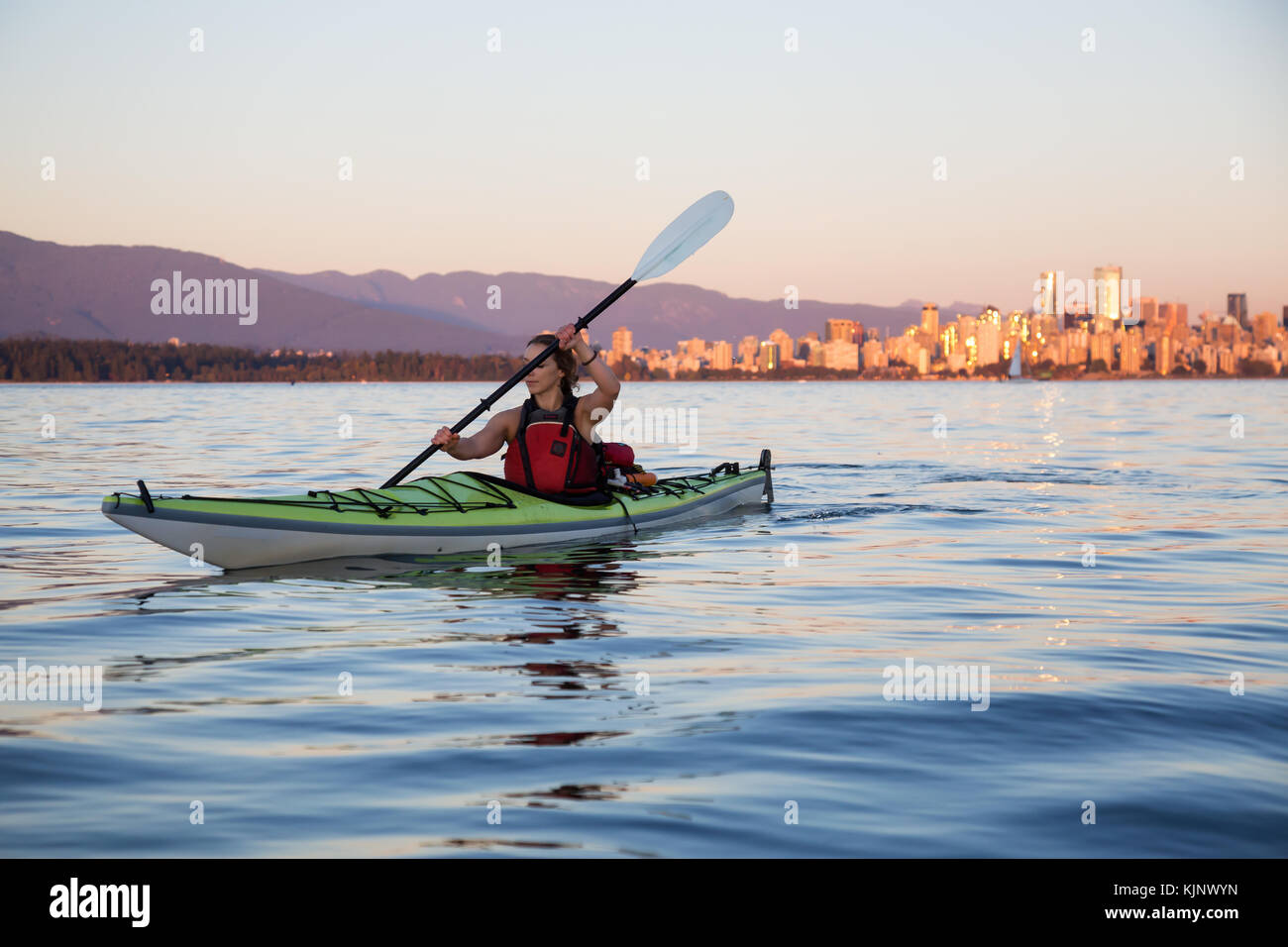 Beautiful woman sea kayaking in the ocean during a colorful and vibrant ...