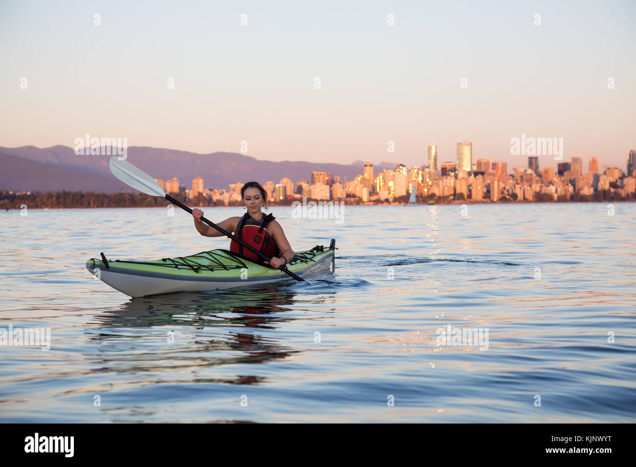 Beautiful woman sea kayaking in the ocean during a colorful and vibrant ...