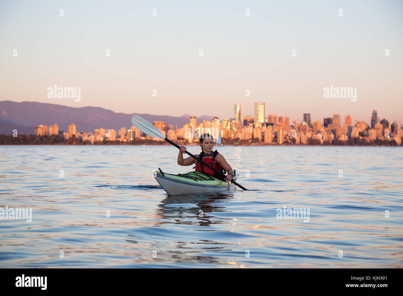 Beautiful woman sea kayaking in the ocean during a colorful and vibrant ...
