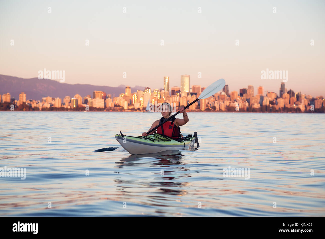 Beautiful woman sea kayaking in the ocean during a colorful and vibrant ...