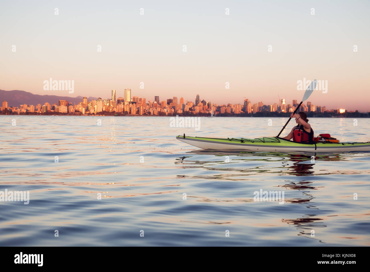 Beautiful woman sea kayaking in the ocean during a colorful and vibrant ...