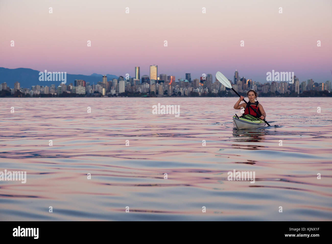 Beautiful woman sea kayaking in the ocean during a colorful and vibrant ...