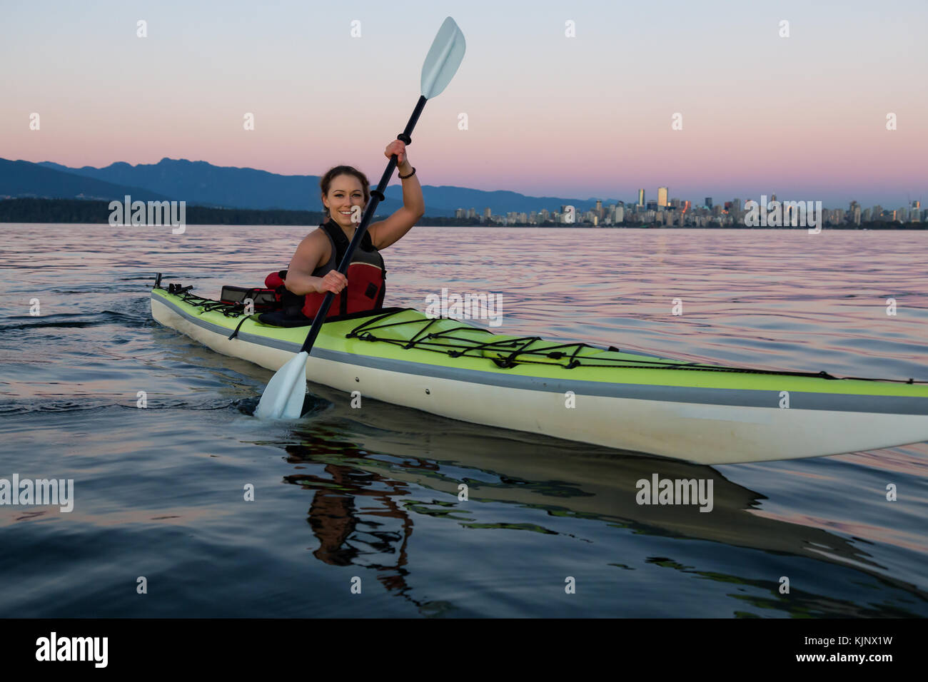 Beautiful woman sea kayaking in the ocean during a colorful and vibrant ...