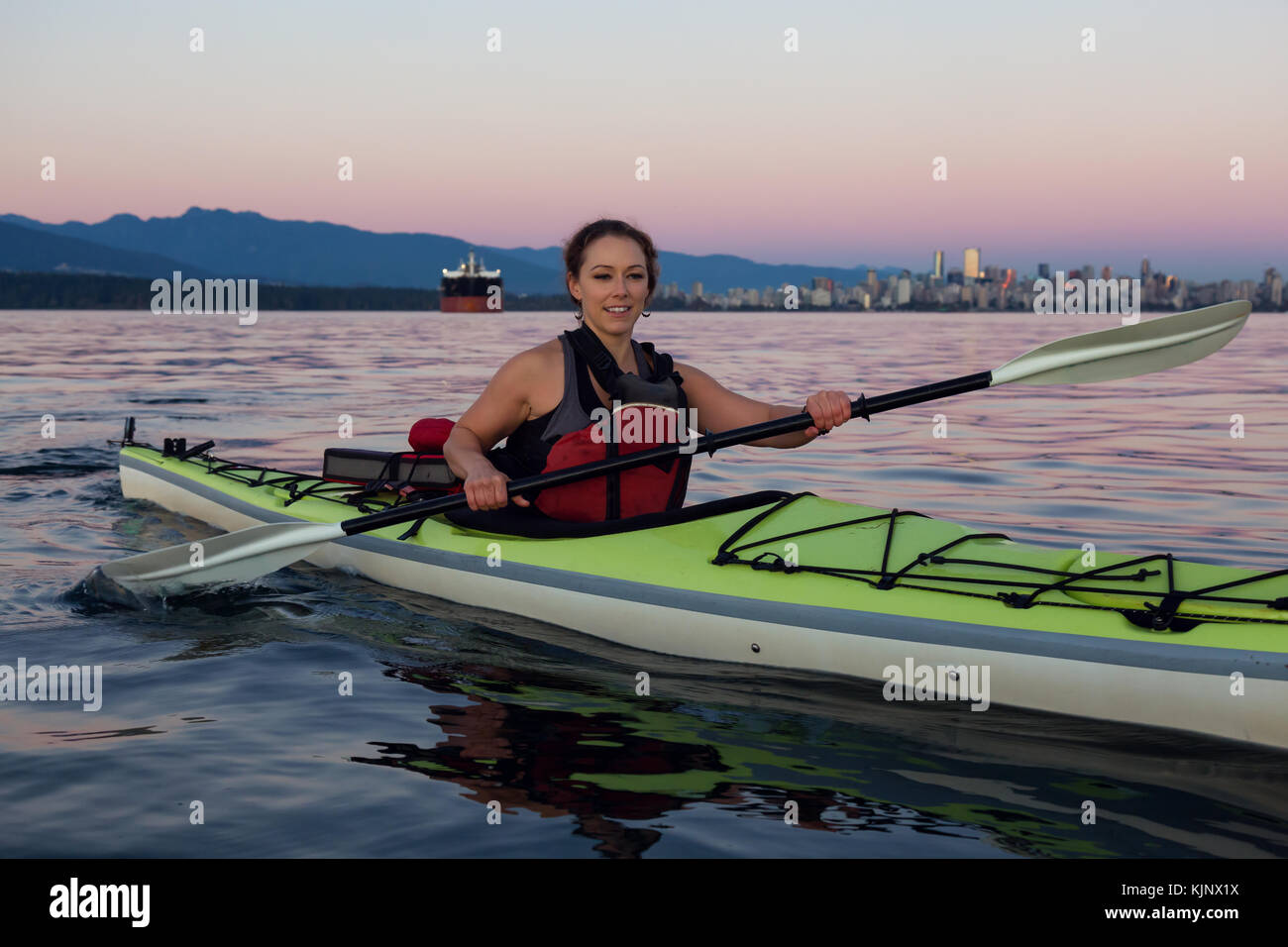 Beautiful woman sea kayaking in the ocean during a colorful and vibrant ...