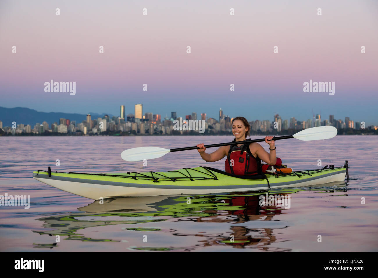 Beautiful woman sea kayaking in the ocean during a colorful and vibrant ...