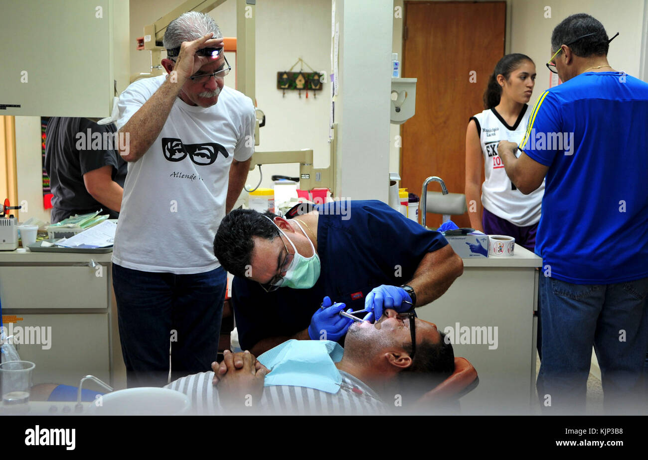 A dentist works on a patient while a volunteer provides overhead ...