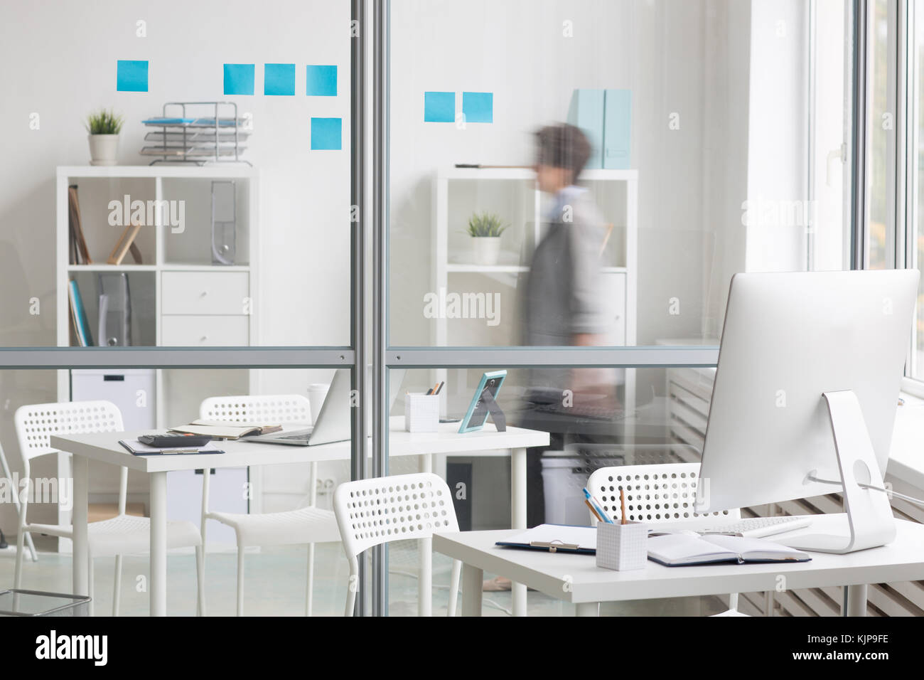 Blurred human figure moving behind transparent wall between two offices ...