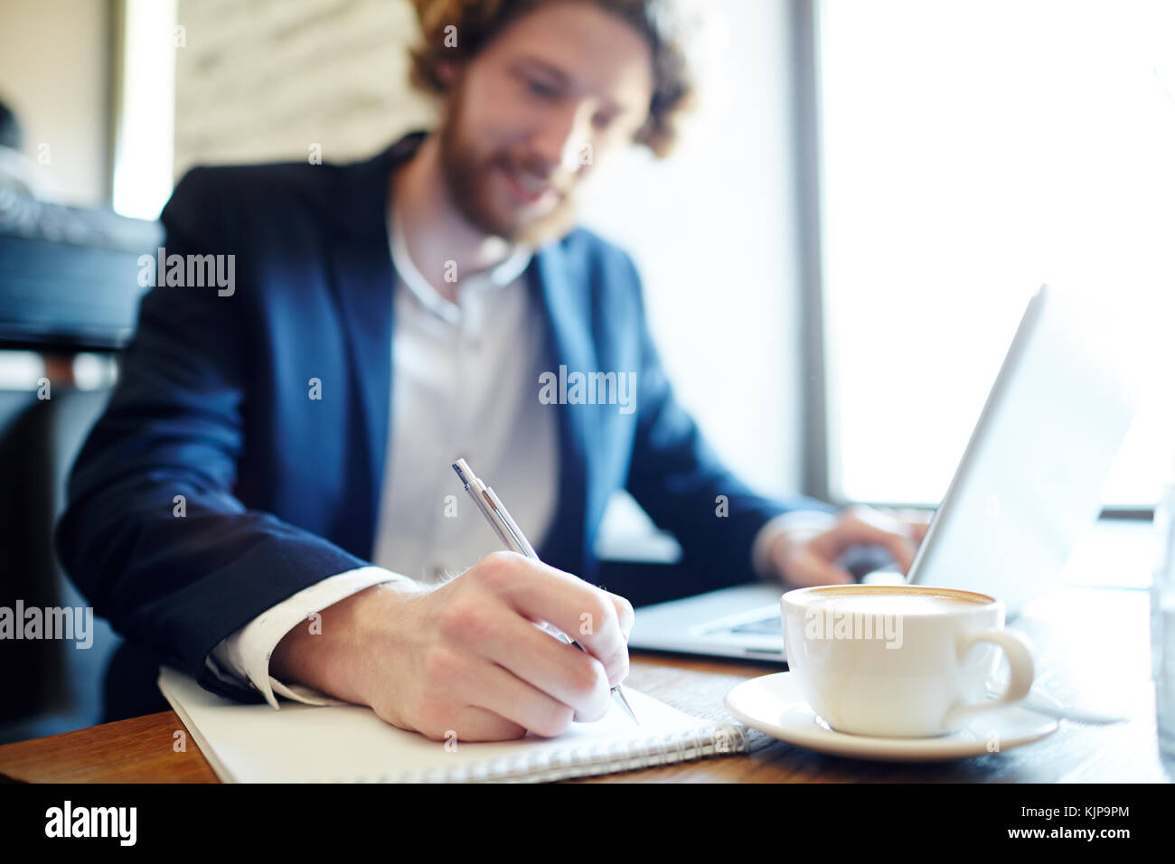 Businessman with pen writing down plan of work in notepad with cup of ...