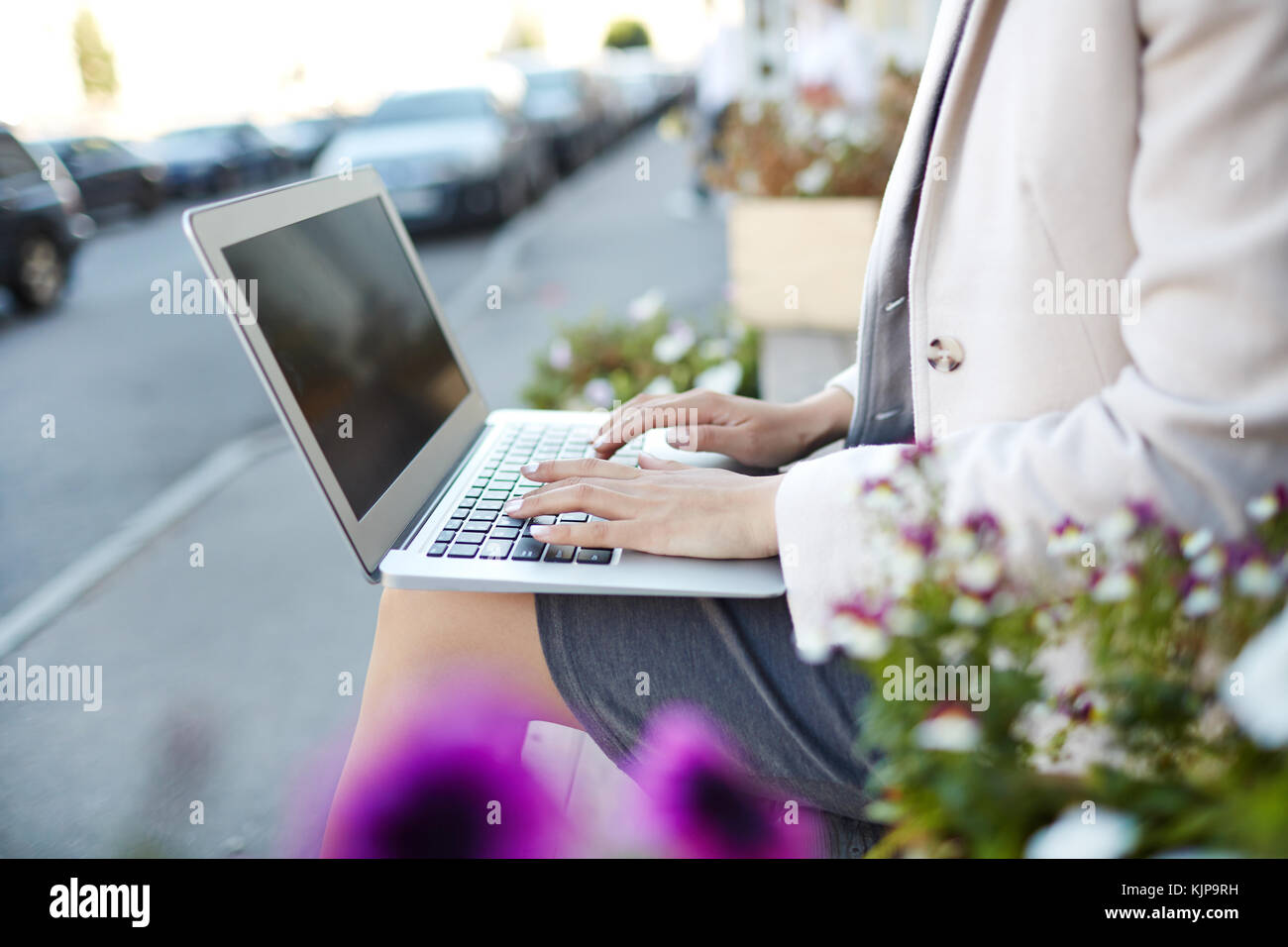Busy female typing on laptop while sitting by flowerbed in the city ...