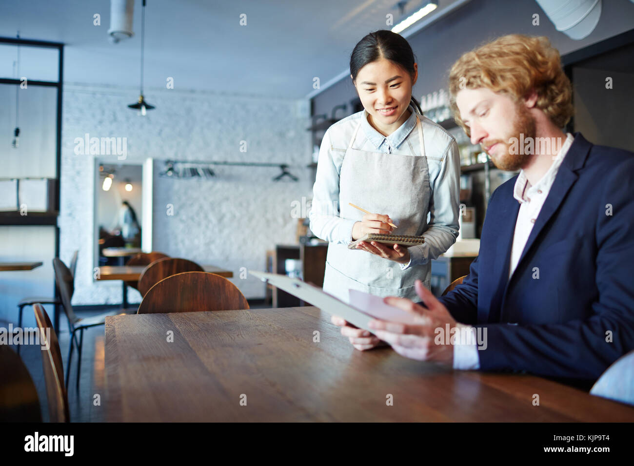 Young businessman reading menu and ordering something for lunch or ...