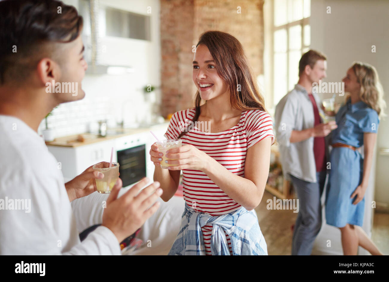 Two young couples with drinks talking at home while gathering together ...