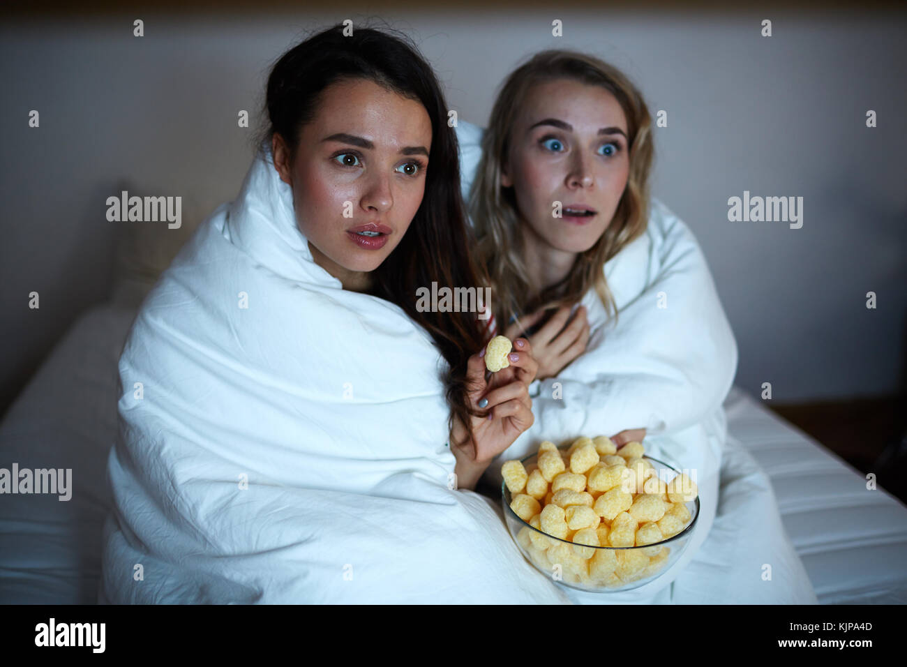 Two girls wrapped into blanket eating corn cheerios and watching horror ...