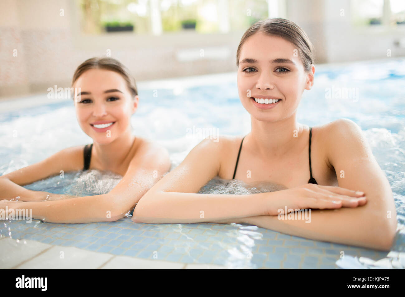 Young smiling women enjoying spa procedure in warm whirlpool at resort ...
