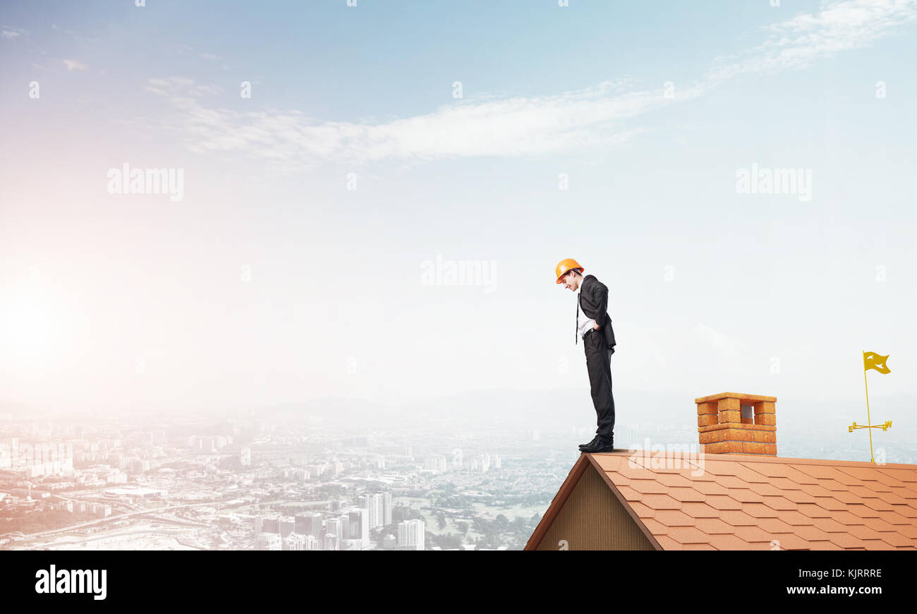 Businessman looking down from roof and modern cityscape at background ...