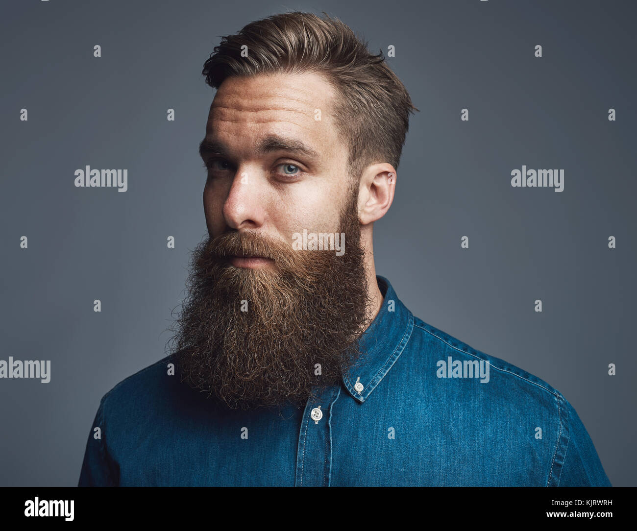 Hip and stylish young man with a long beard standing alone in a studio ...