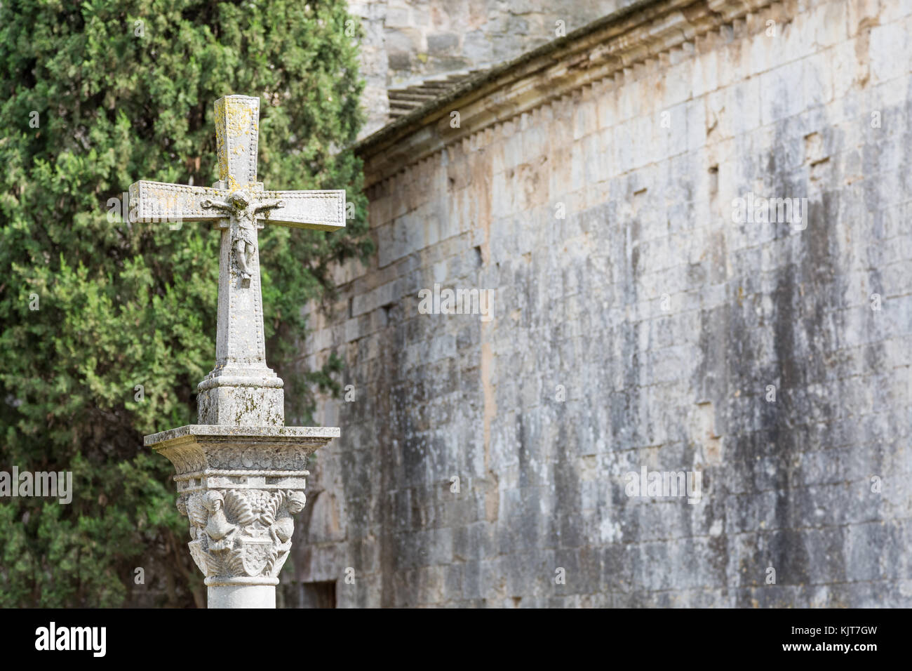 Weathered stone cross with Christ in front of a medieval wall in Girona ...