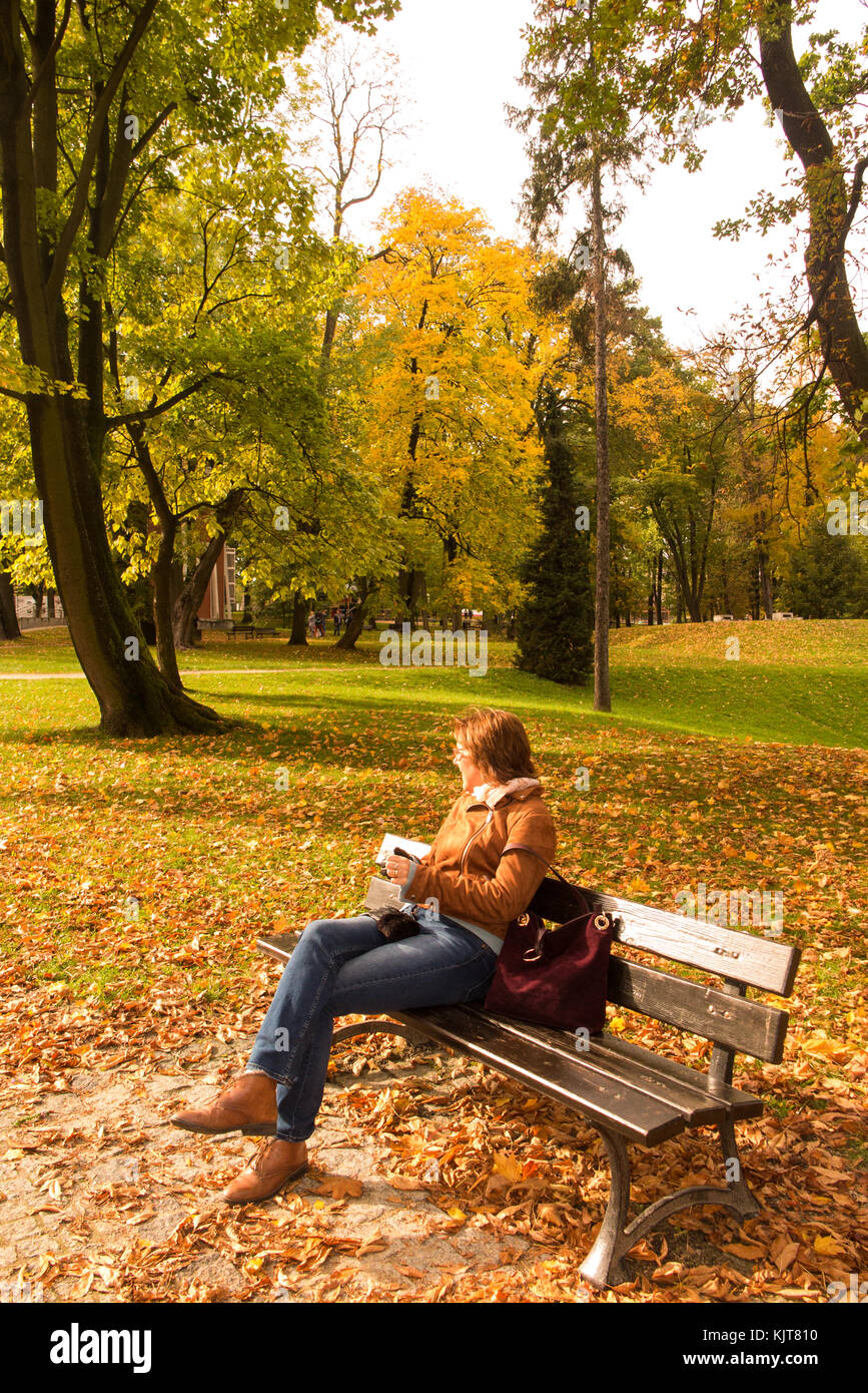 Woman sitting on a park bench in a city parkland and woodland in the ...