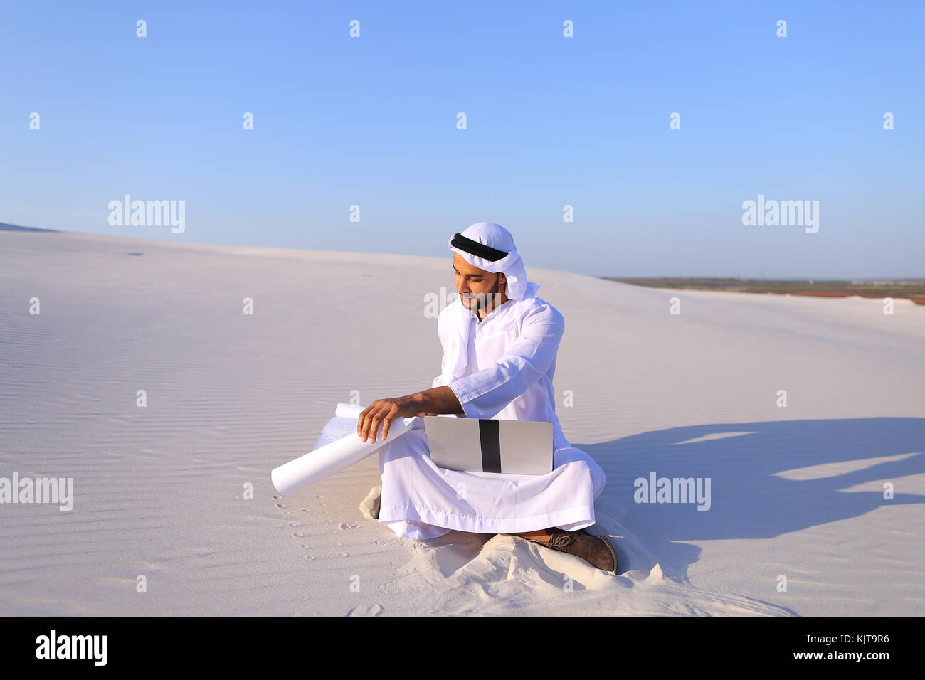 Muslim male architect sitting with laptop on sand in desert on h Stock ...