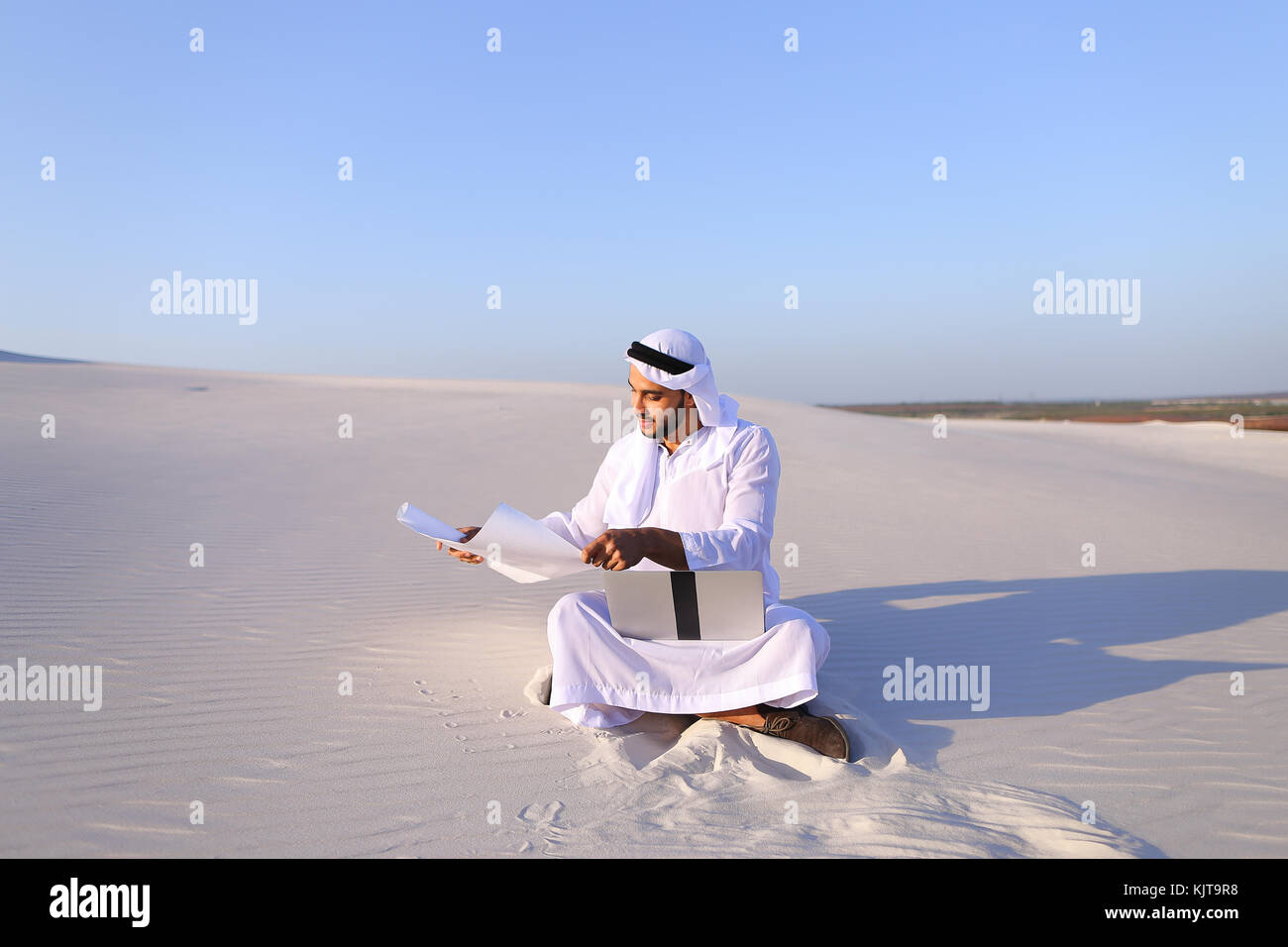 Muslim male architect sitting with laptop on sand in desert on h Stock ...