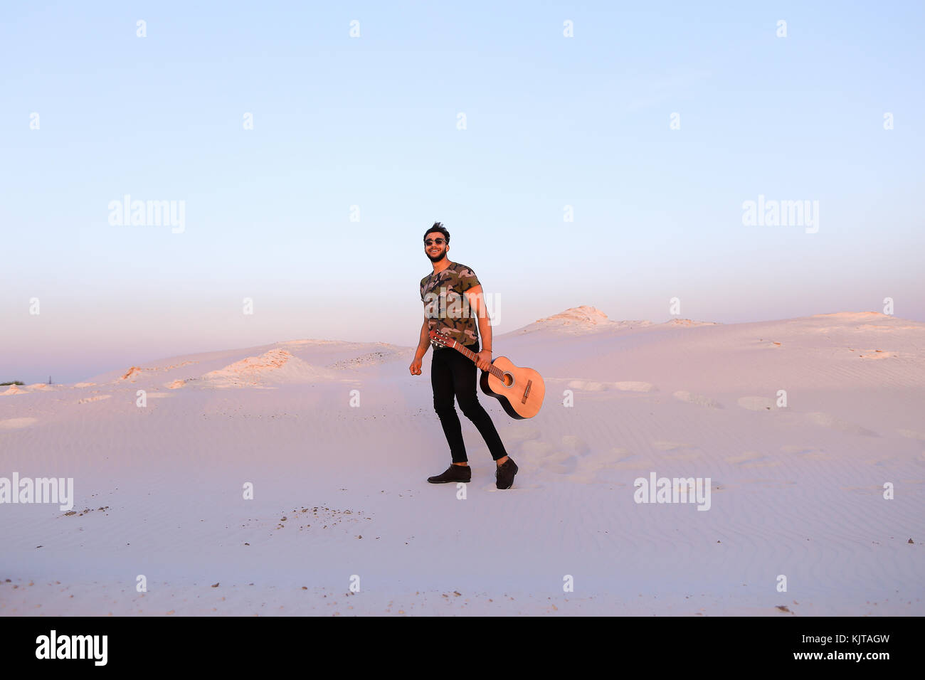 Stately Muslim young man walks with guitar in hands through dese Stock ...