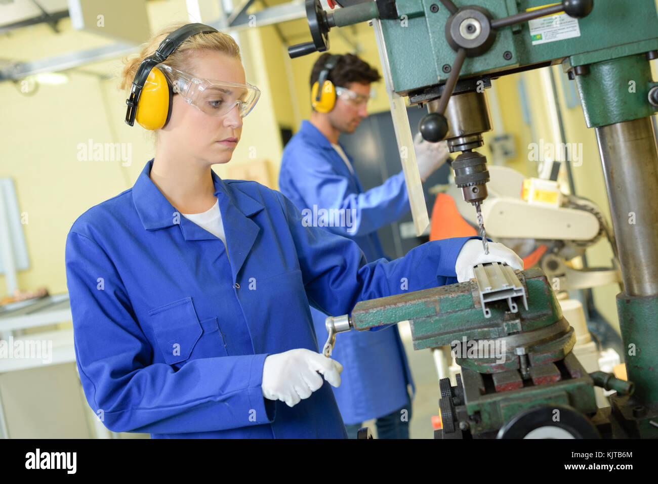 serious trainees focused on drilling metal piece with professional ...