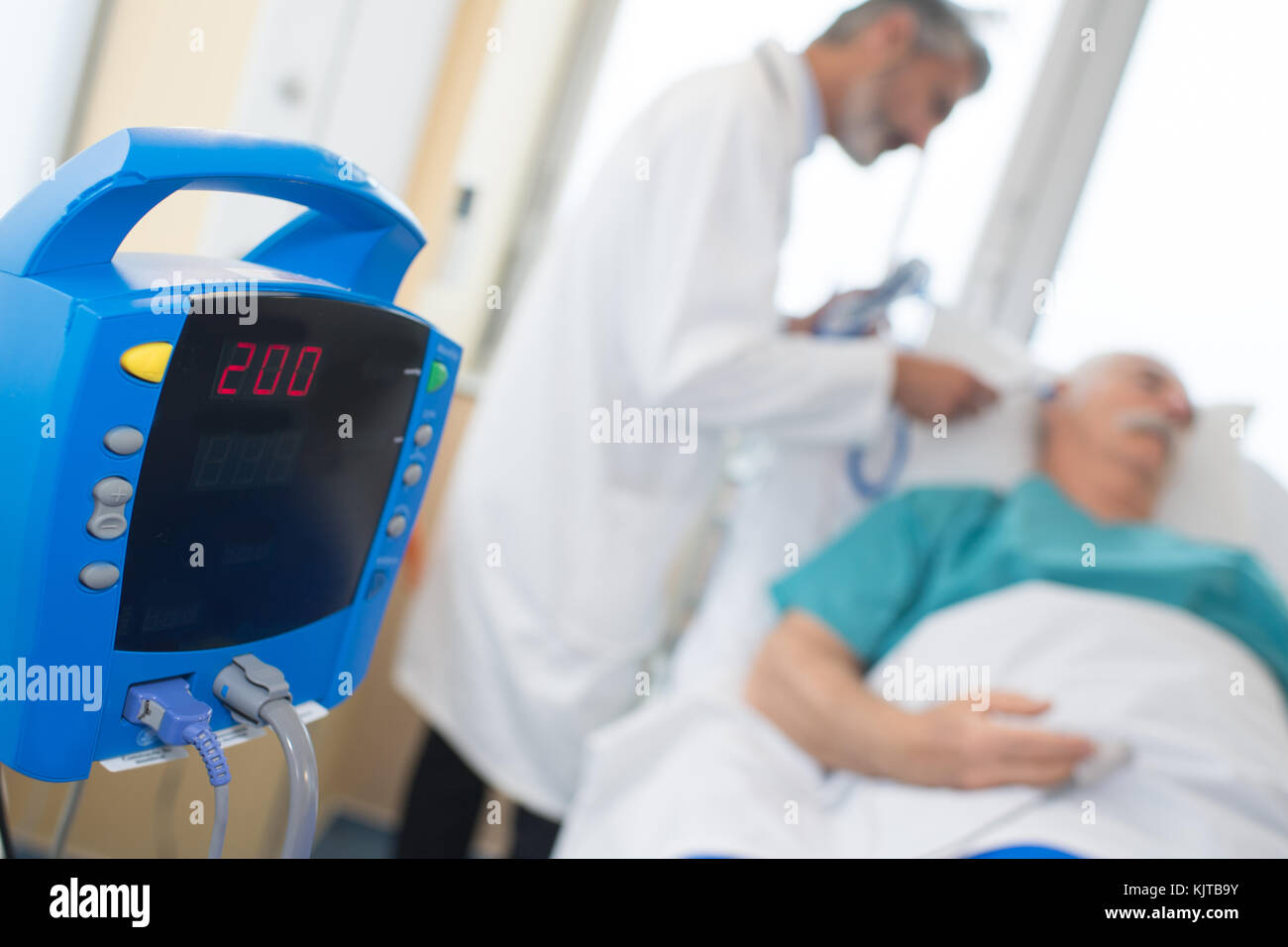 Heart monitor in foreground, patient in hospital bed in background ...