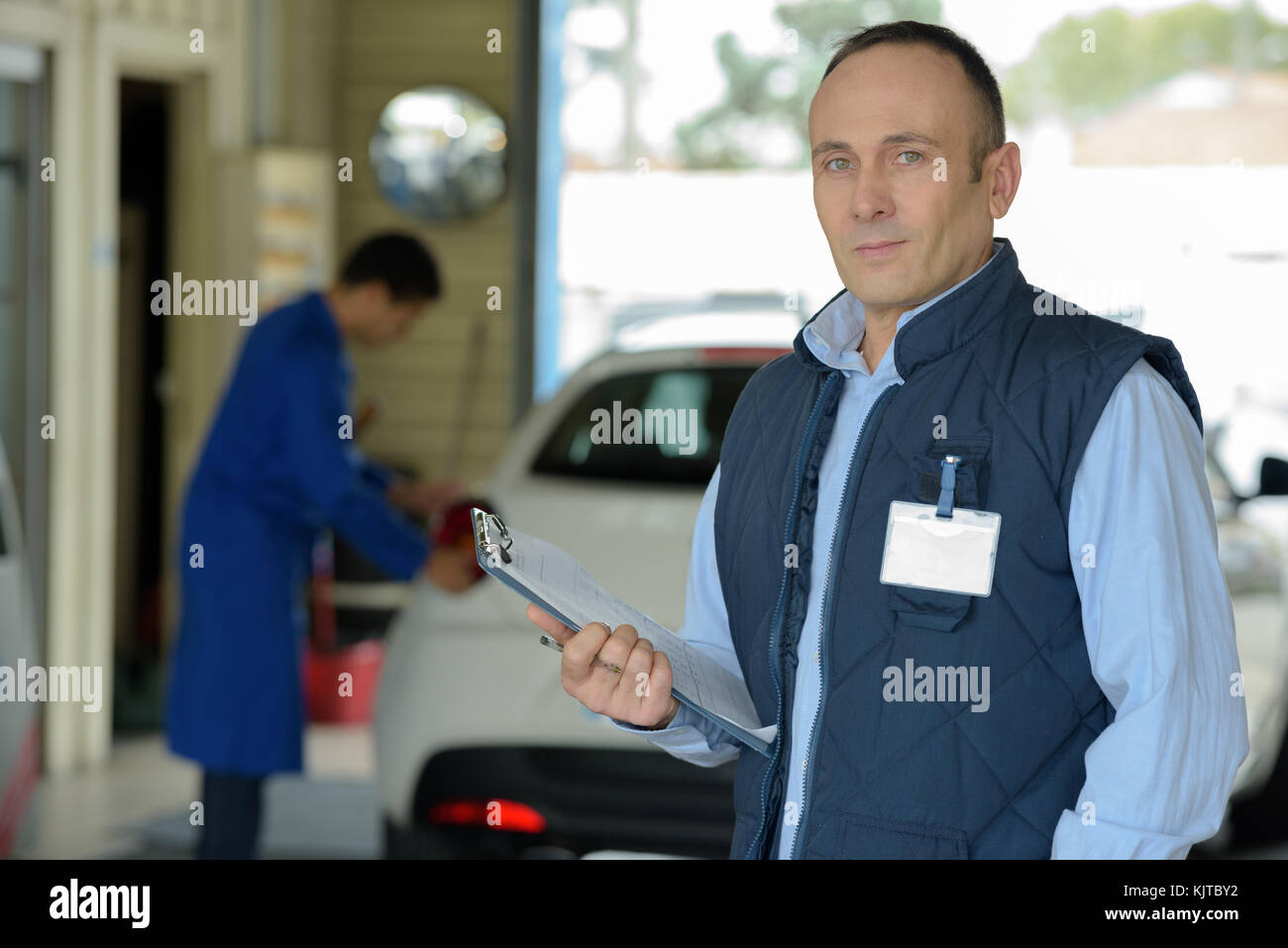 mechanic with a clipboard and pen standing near car Stock Photo - Alamy