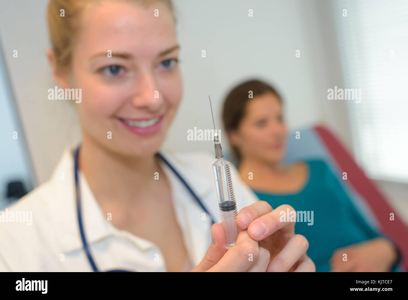 smiling nurse holding syringe female patient in background Stock Photo ...