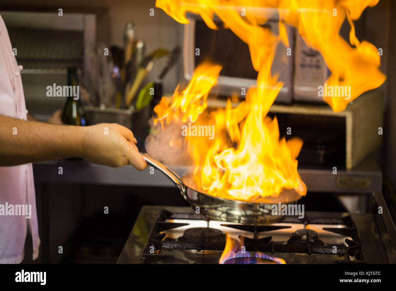 Chef cooking food in flambe style over a gas stove. Natural light and ...