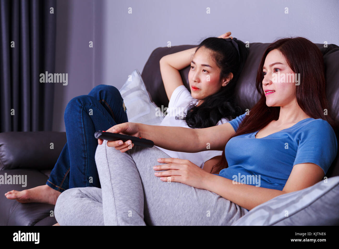 two best friends watching tv with remote on sofa in living room at home ...