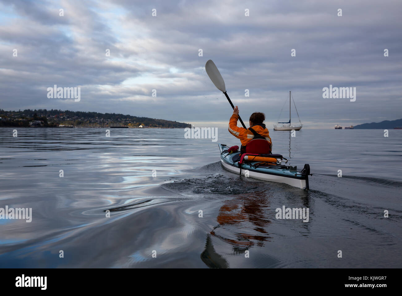 Woman kayaking in the ocean during a vibrant and cloudy morning. Taken ...