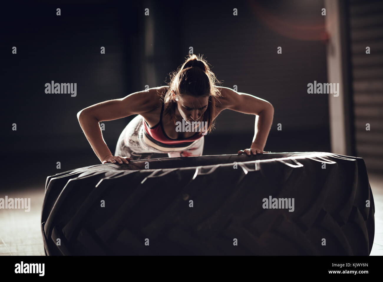 Young muscular woman doing push-up exercise on a tire at cross fit ...