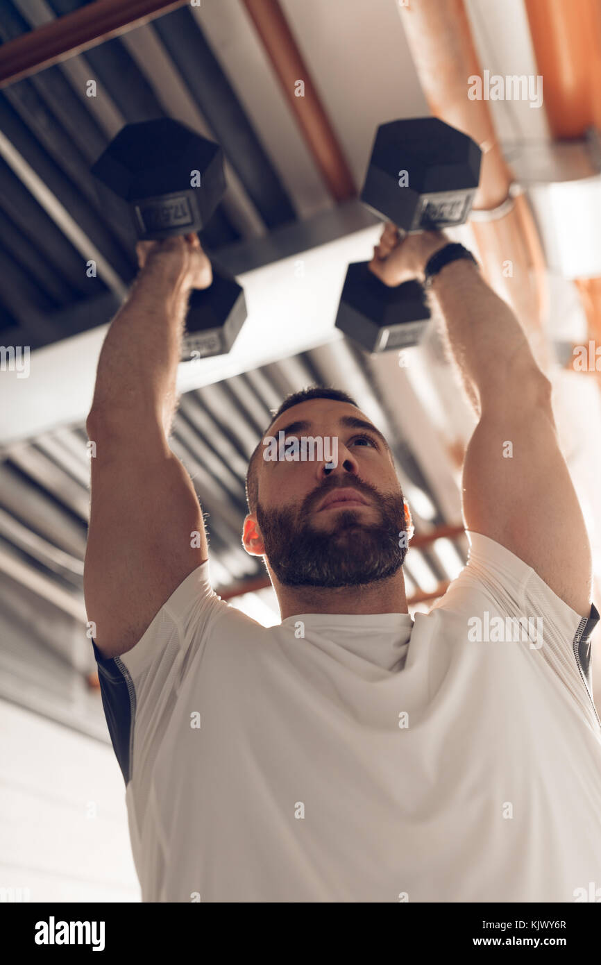 Young muscular man doing hard exercise with dumbbells for shoulders on ...