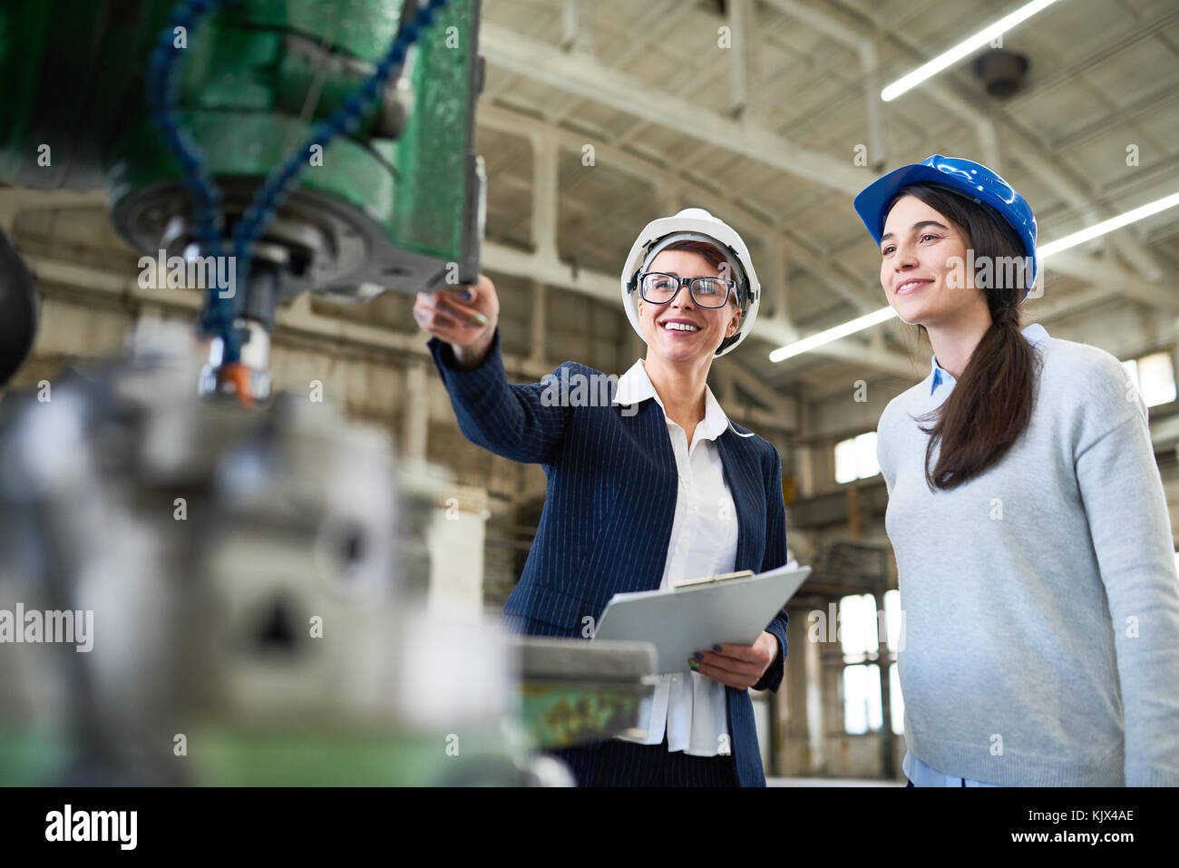 Cheerful lady boss presenting factory machine to inspector and sharing ...